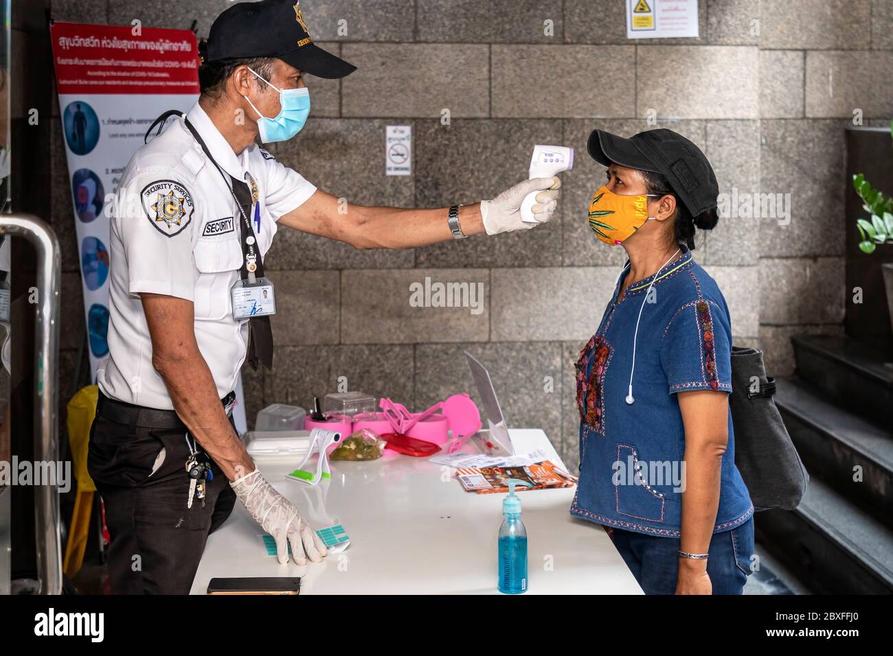 Security guard with face mask checking temperature during Covid ...