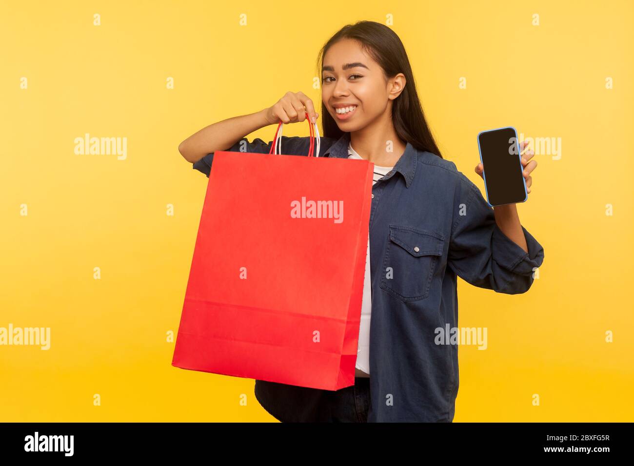 Portrait of happy shopper girl in stylish denim shirt holding bags and ...