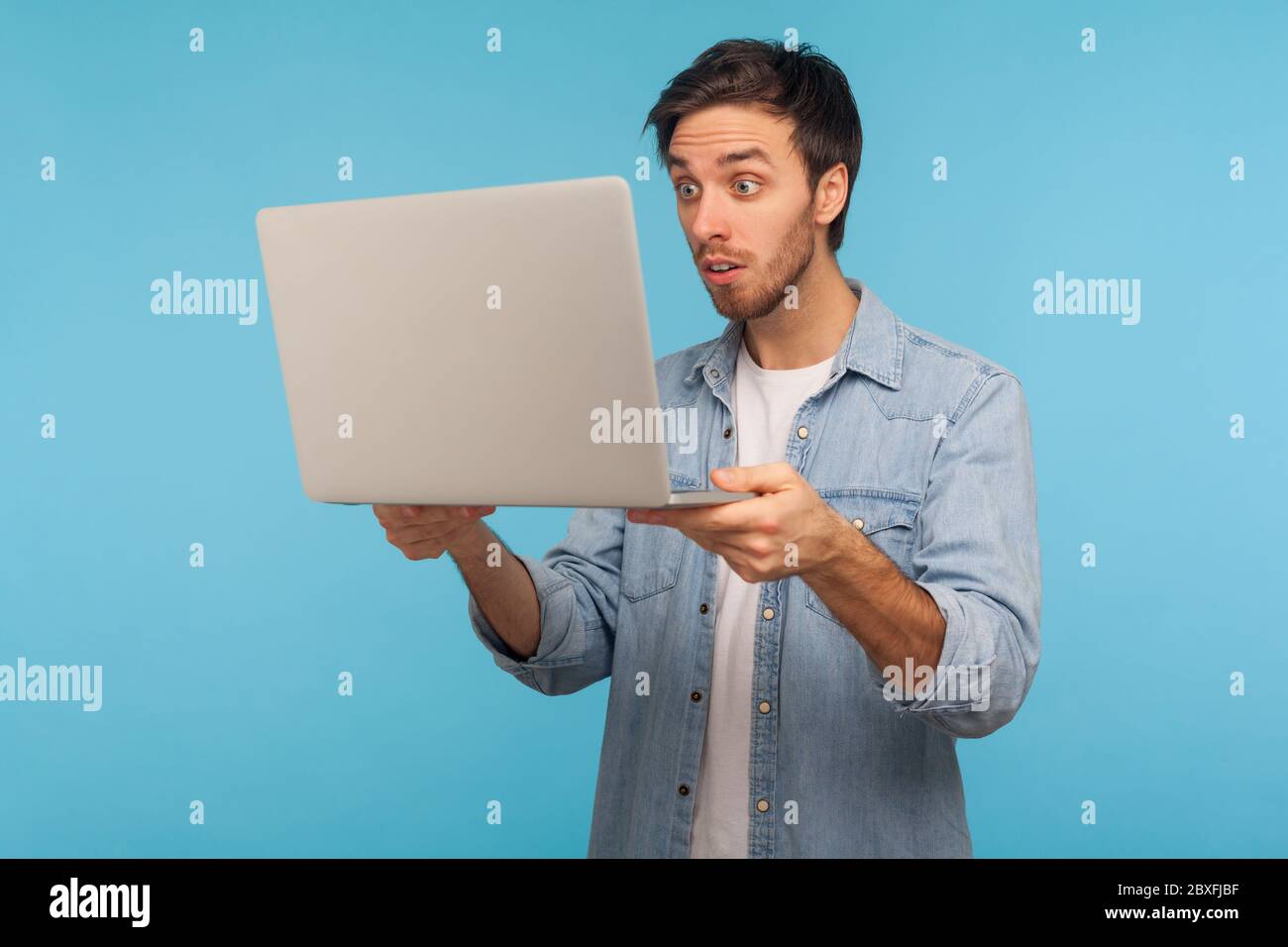 Portrait of funny man in worker denim shirt looking at laptop screen ...