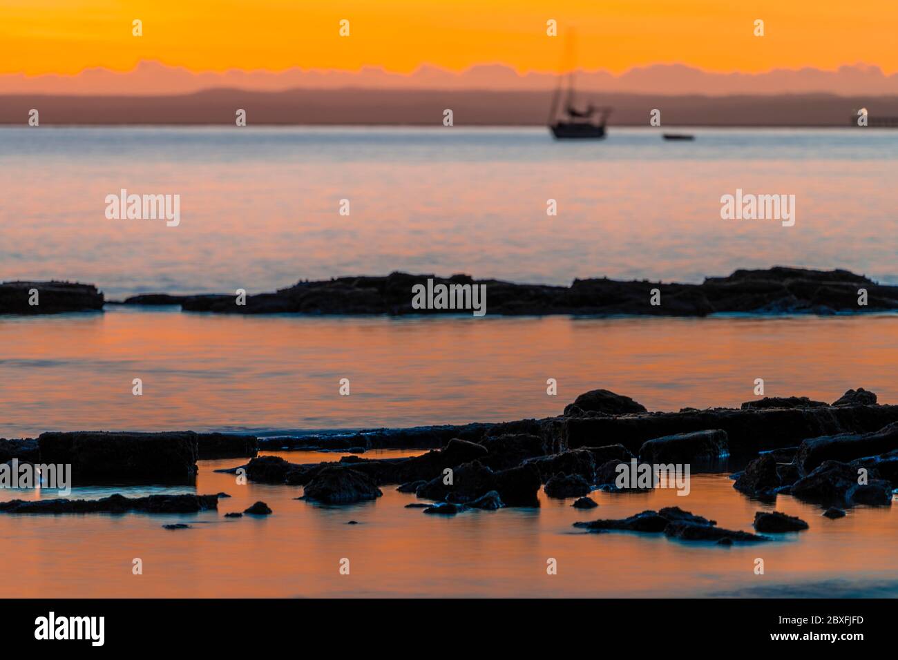 Rocks with sailing ship in background in early morning light Stock ...