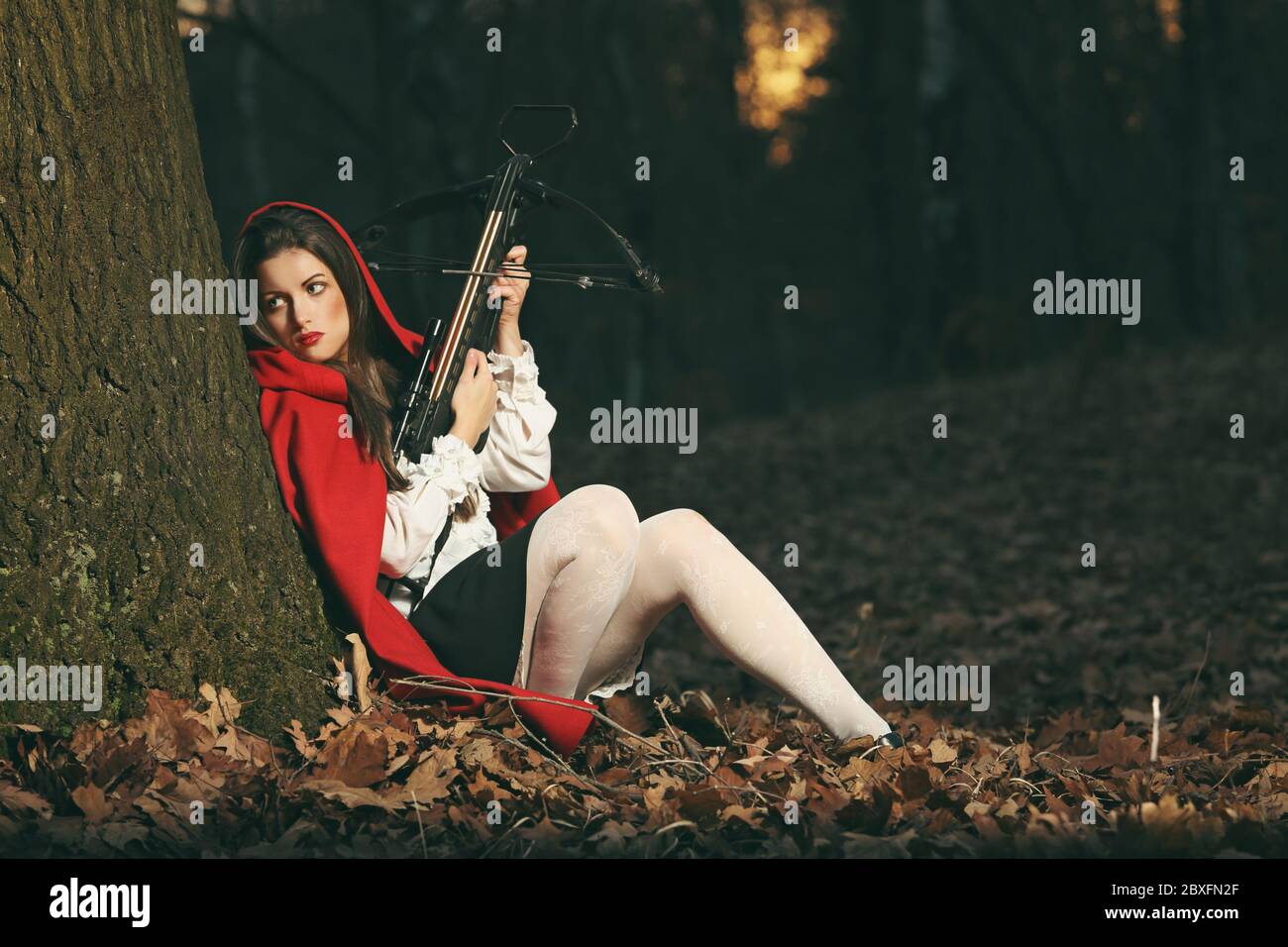 Little red riding hood leaning to a tree in the forest with a crossbow ...