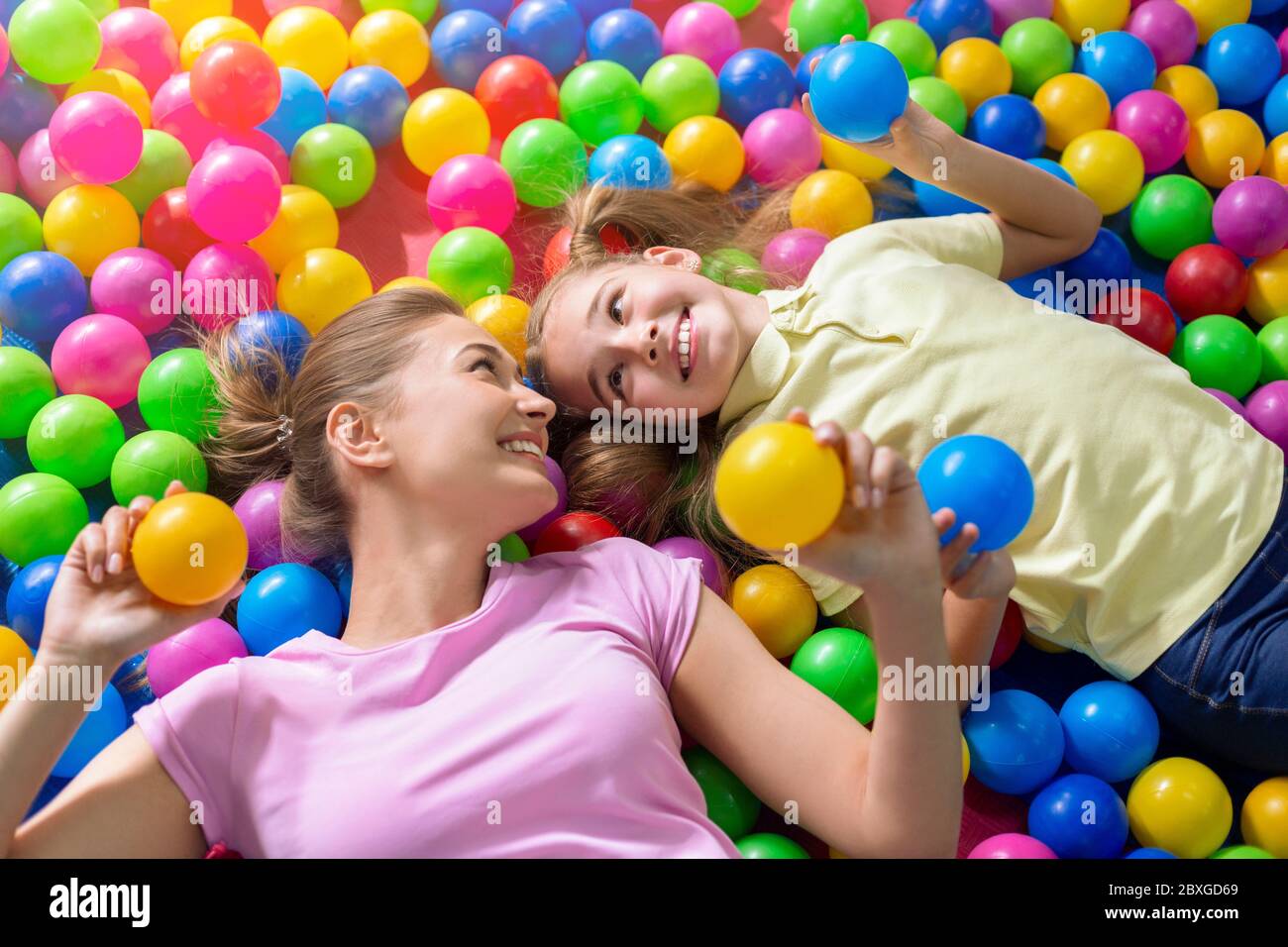 Happy mother and daughter lying in ball pit at indoor kids playground ...