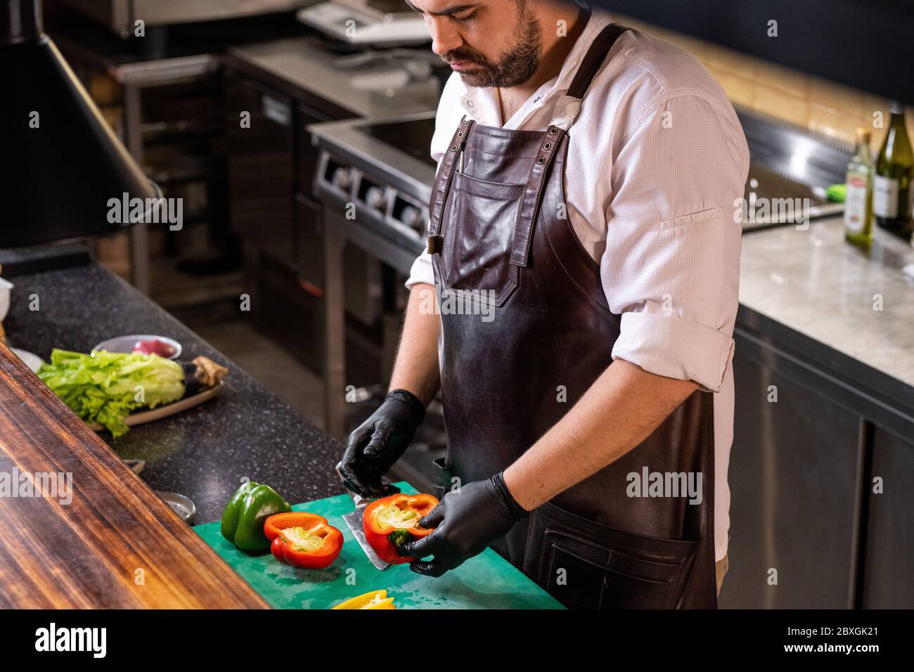 Busy bearded chef in apron standing at counter and making vegetable ...