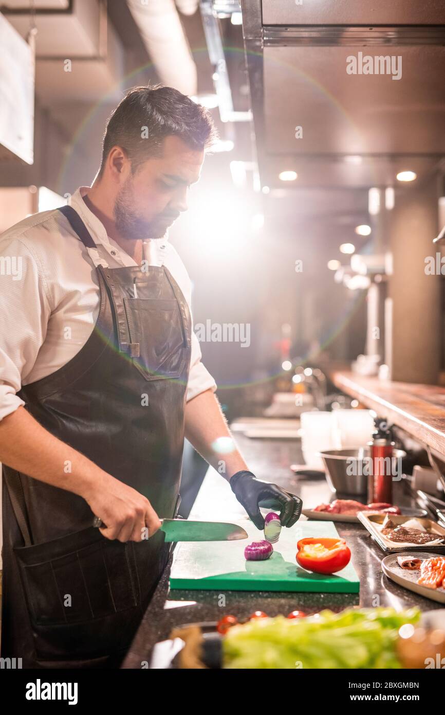 Serious bearded chef working at commercial kitchen and cutting red ...