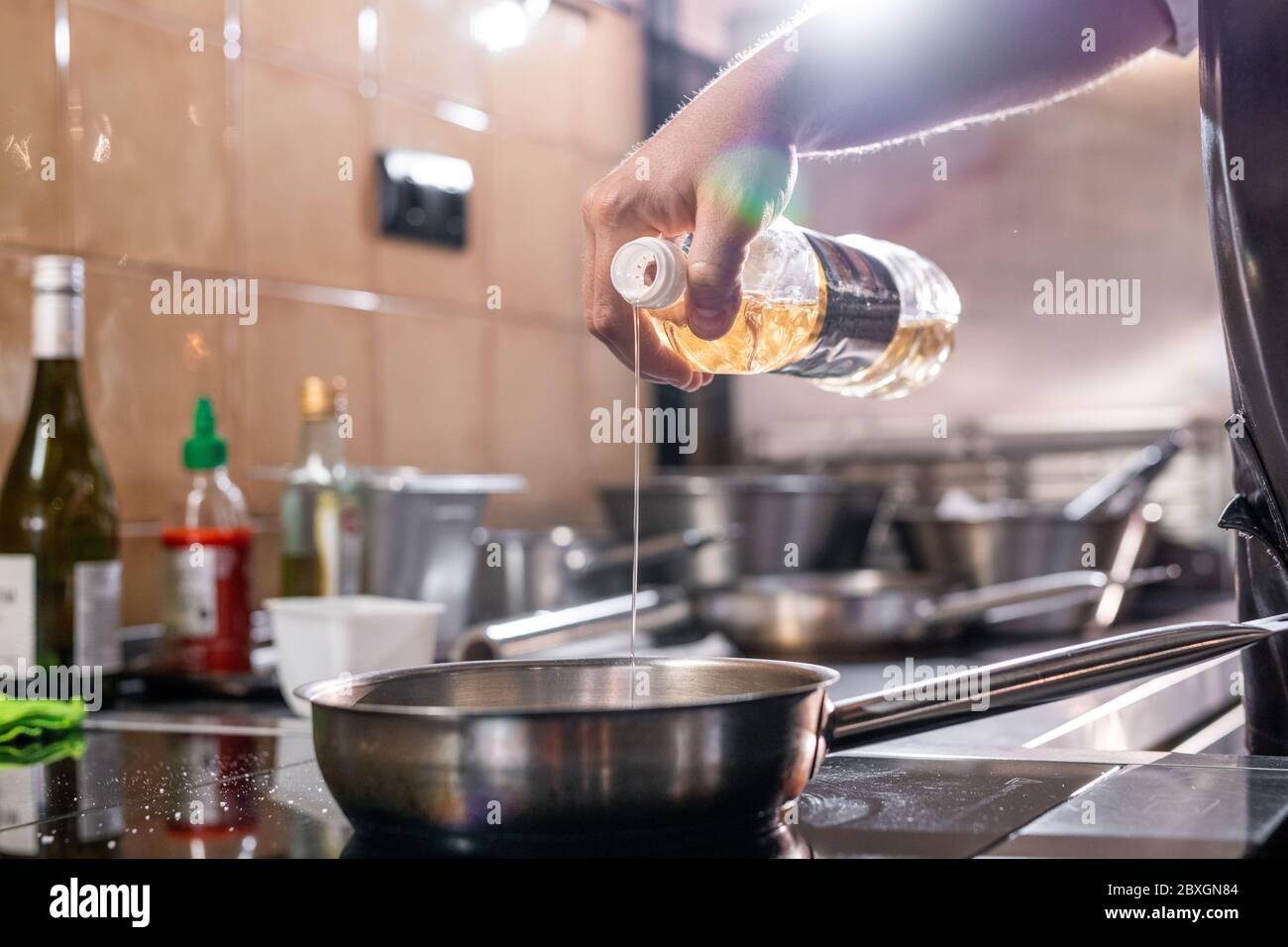 Close-up of unrecognizable chef standing at stove and pouring oil into ...