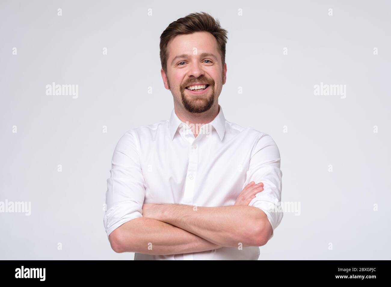 Smart serious young man smiling standing against white background Stock ...