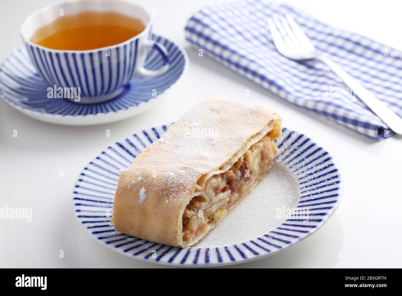 Slice of strudel under powdered sugar and a cup of tea Stock Photo - Alamy