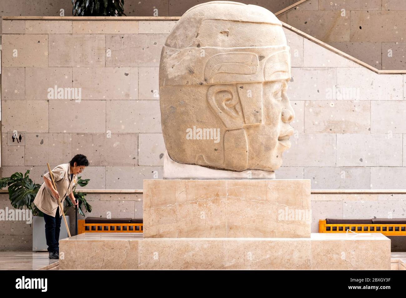 A cleaning woman sweeps around a colossal Olmec stone head at the ...