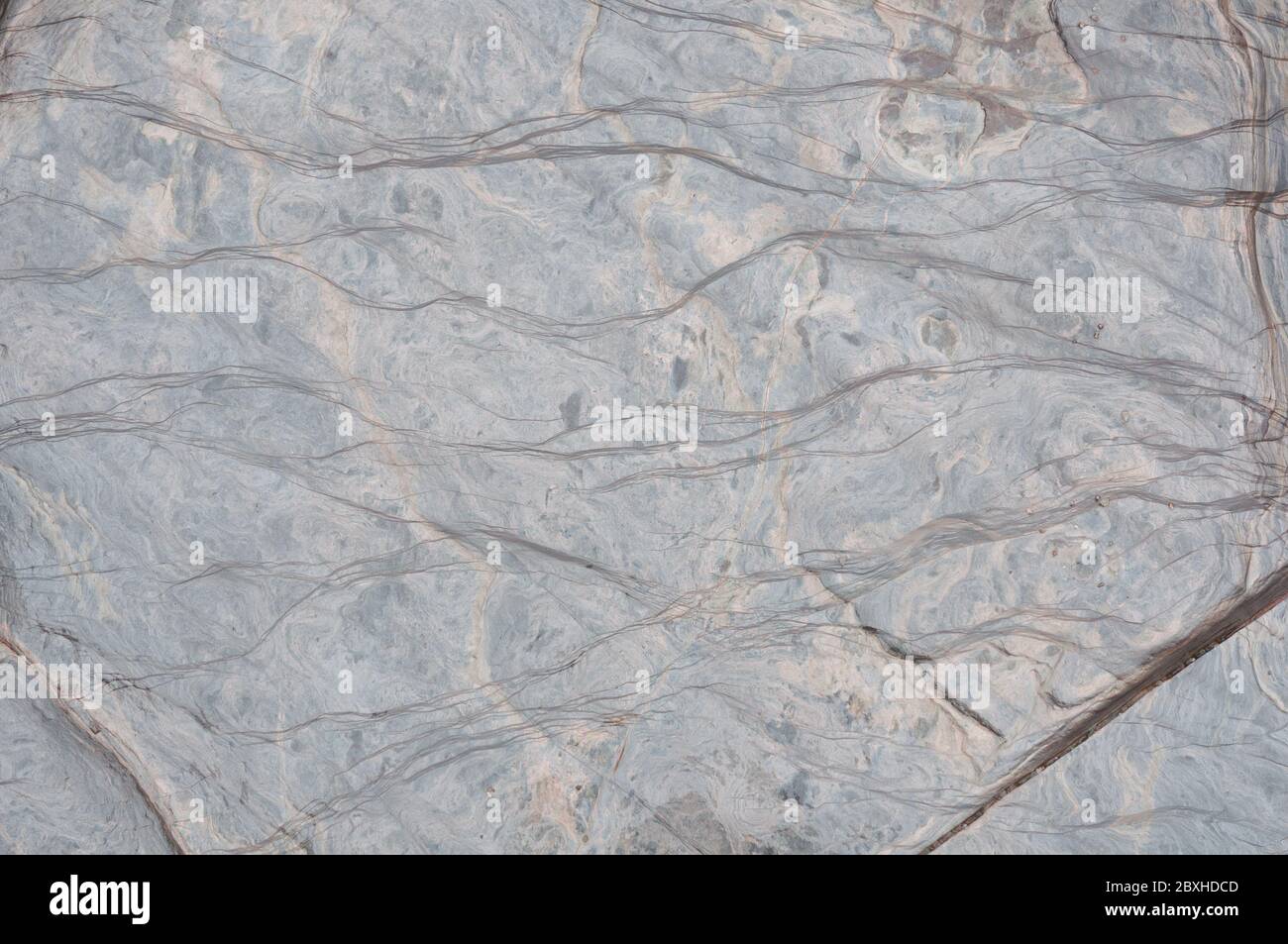 Surface patterns of erosion on a smooth and shiny grey rock look like ...
