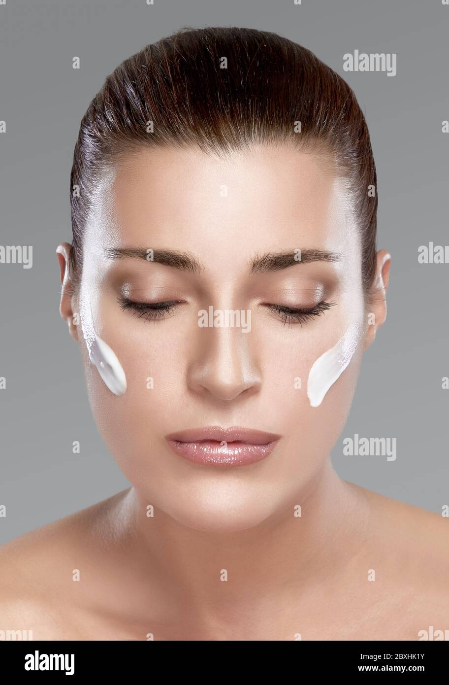 Beautiful spa woman with cream on her face looking down. Perfect skin ...