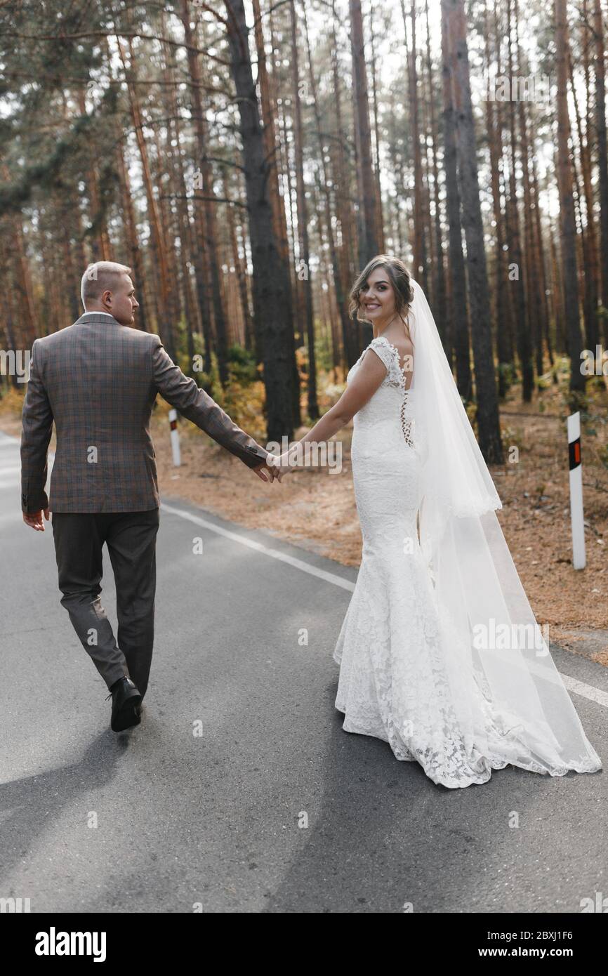 Smiling bride and groom going on the road in the forest photographed ...