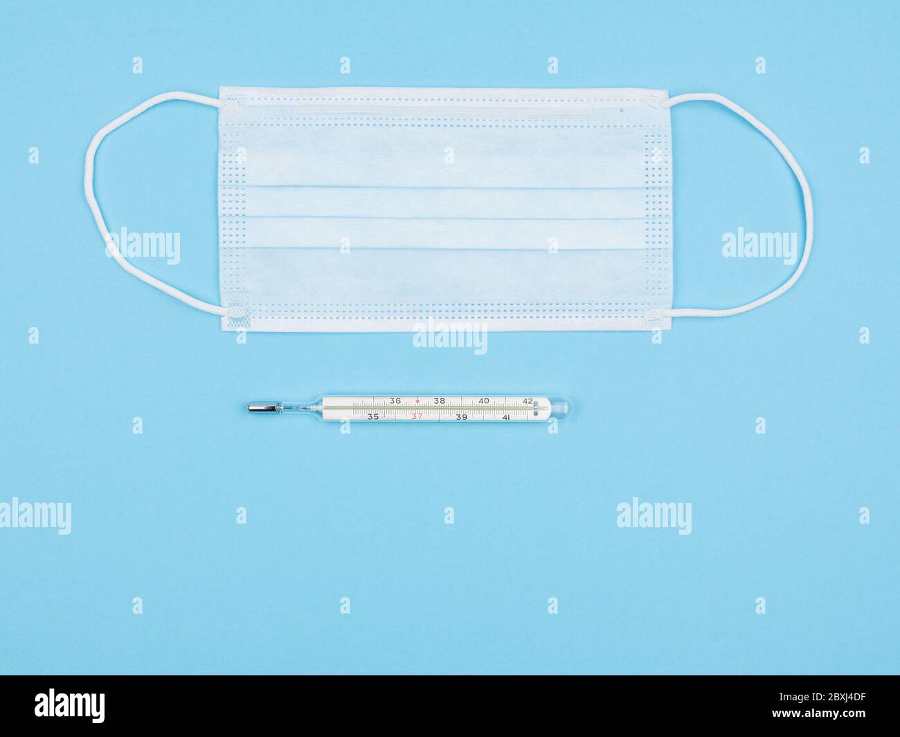 Medical disposable face mask and a mercury thermometer on a blue ...