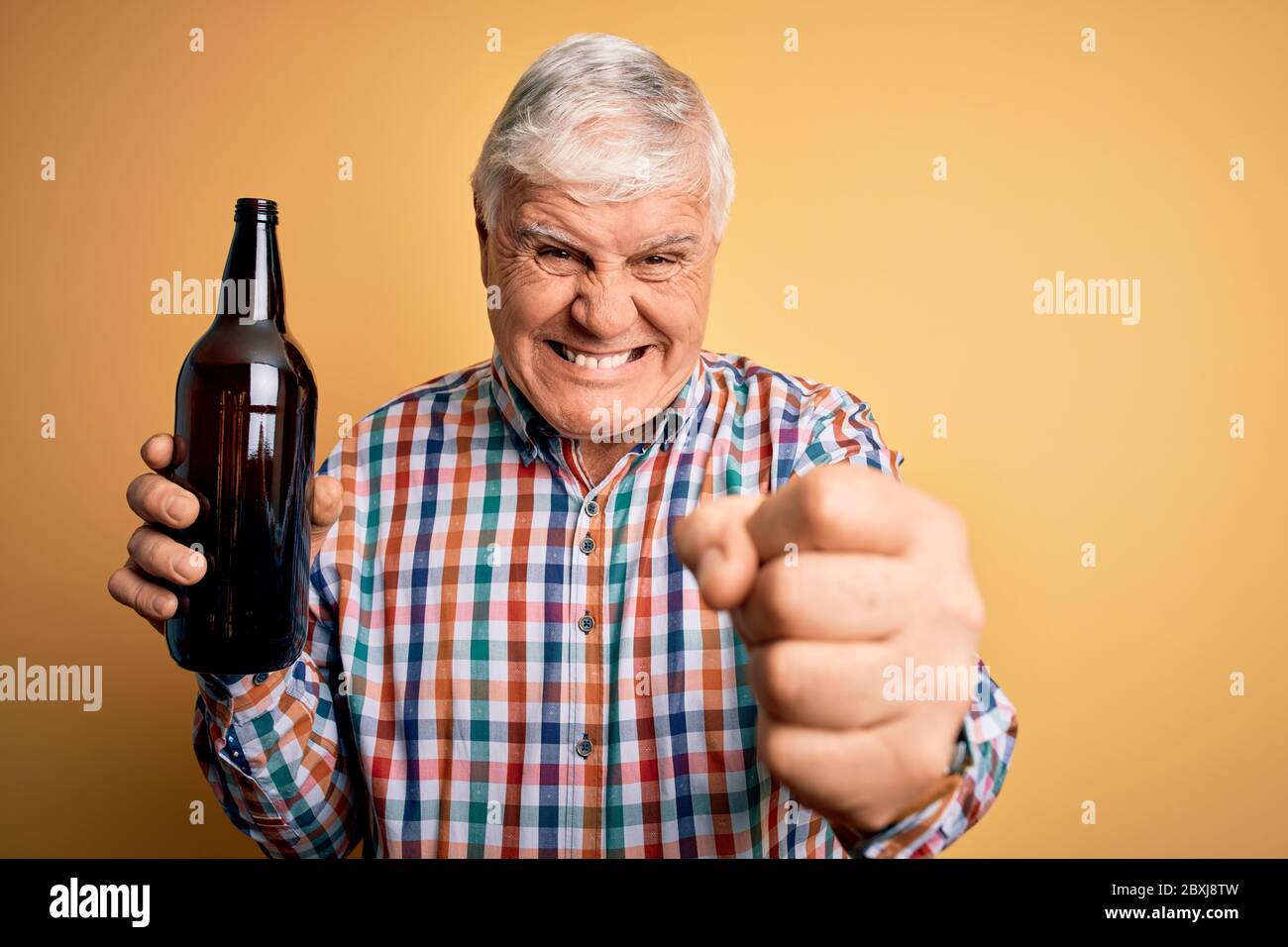 Senior handsome hoary man drinking bottle of beer standing over ...