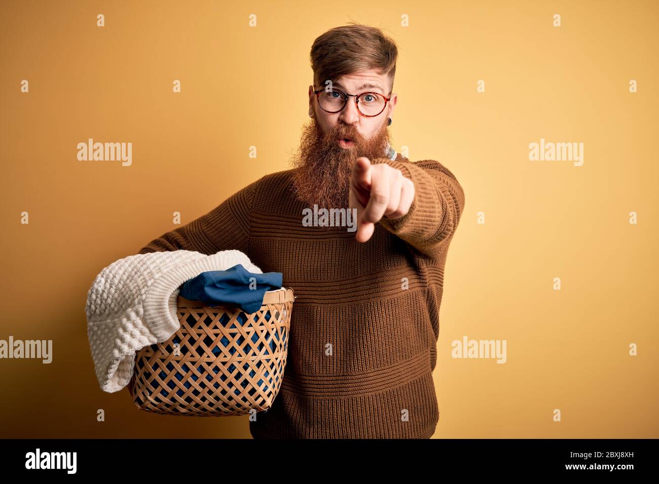Redhead Irish Man With Beard Doing Housework Laundry Over Yellow Background Pointing With Finger