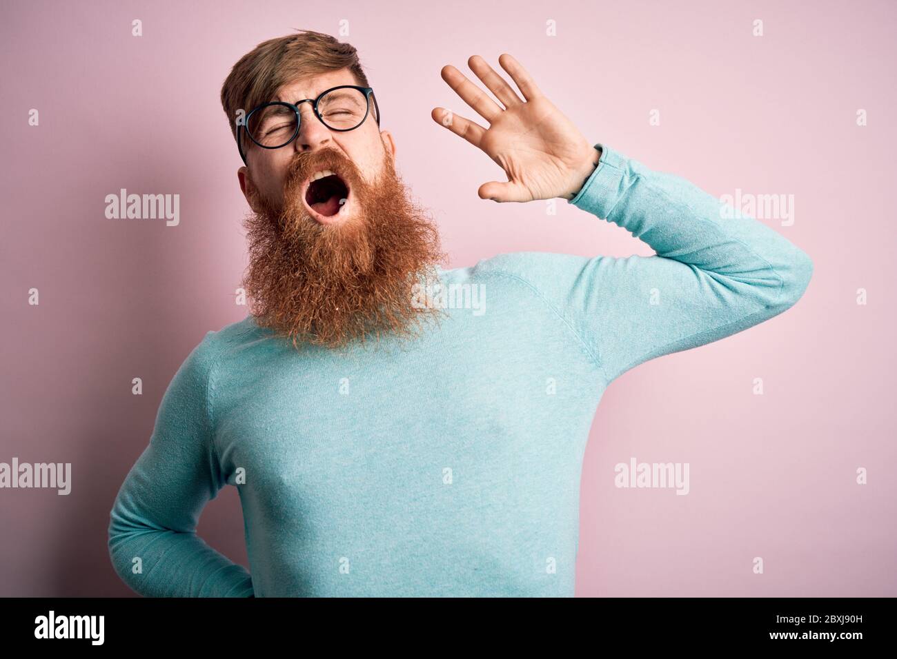Handsome Irish redhead man with beard wearing glasses over pink ...