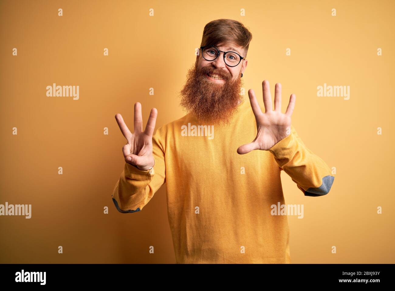 Handsome Irish redhead man with beard wearing glasses over yellow ...
