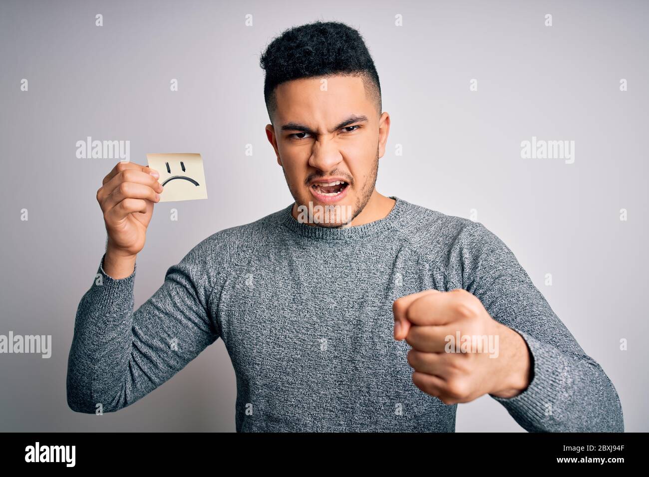 Handsome man holding reminder paper with sad emotion face emoji over ...