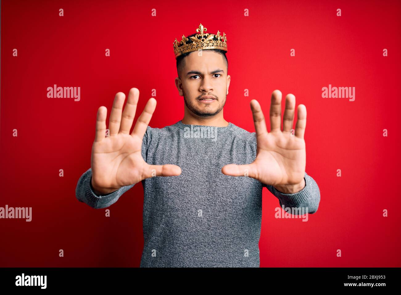 Young handsome man wearing golden crown of prince over isolated red ...