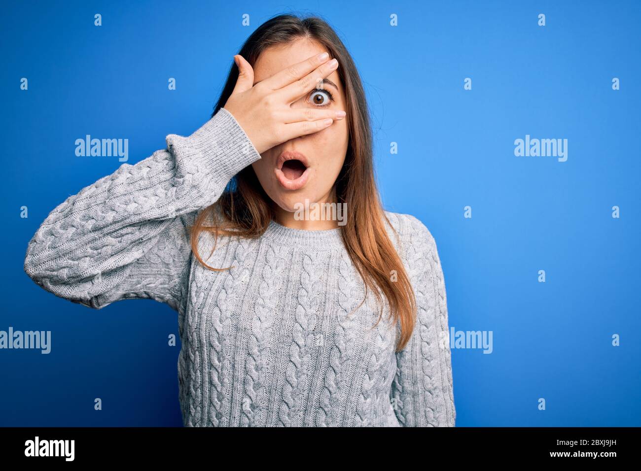 Beautiful young woman wearing casual wool sweater standing over blue ...