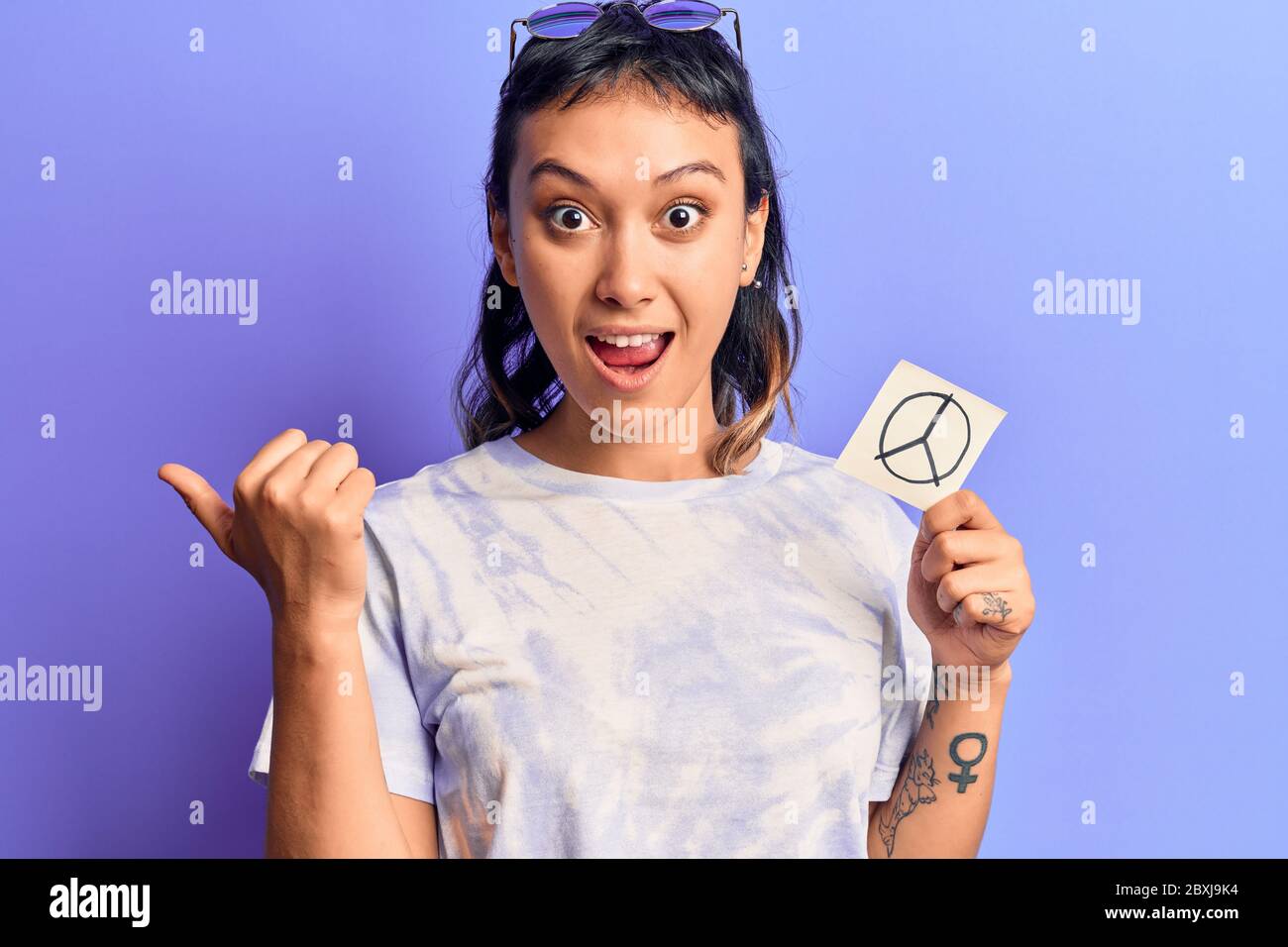 Young woman holding peace symbol reminder paper pointing thumb up to ...