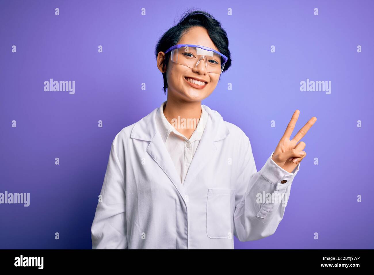 Young beautiful asian scientist girl wearing coat and glasses over ...