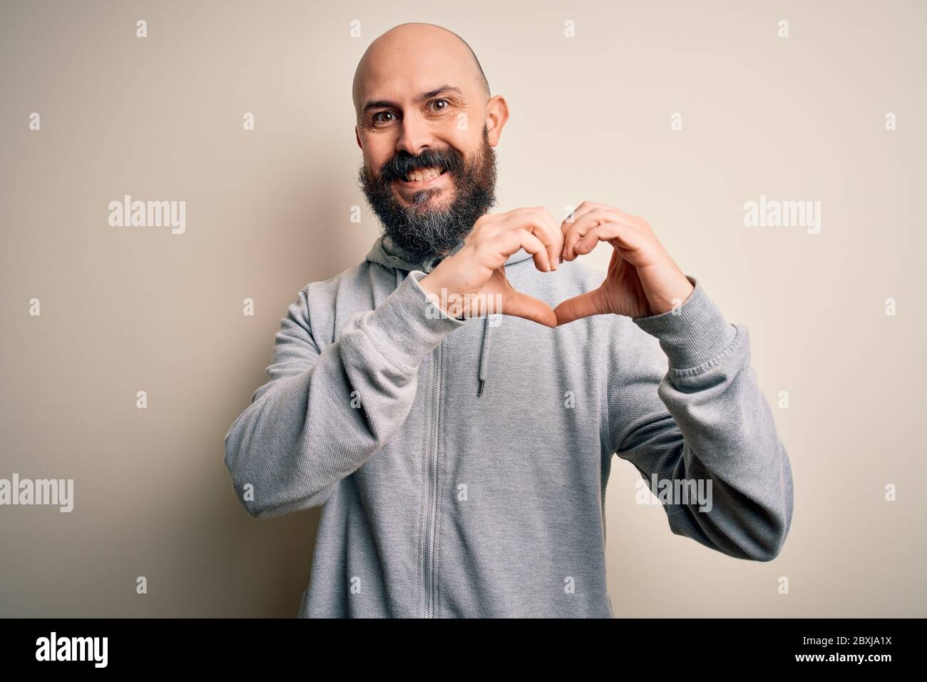 Handsome sporty bald man with beard wearing sweatshirt standing over ...