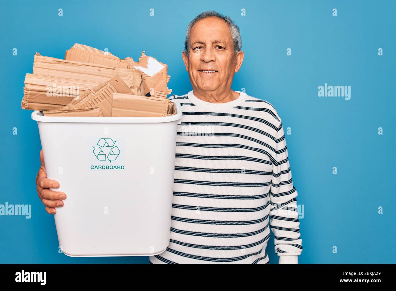 Senior man recycling holding trash can with cardboard to recycle over ...