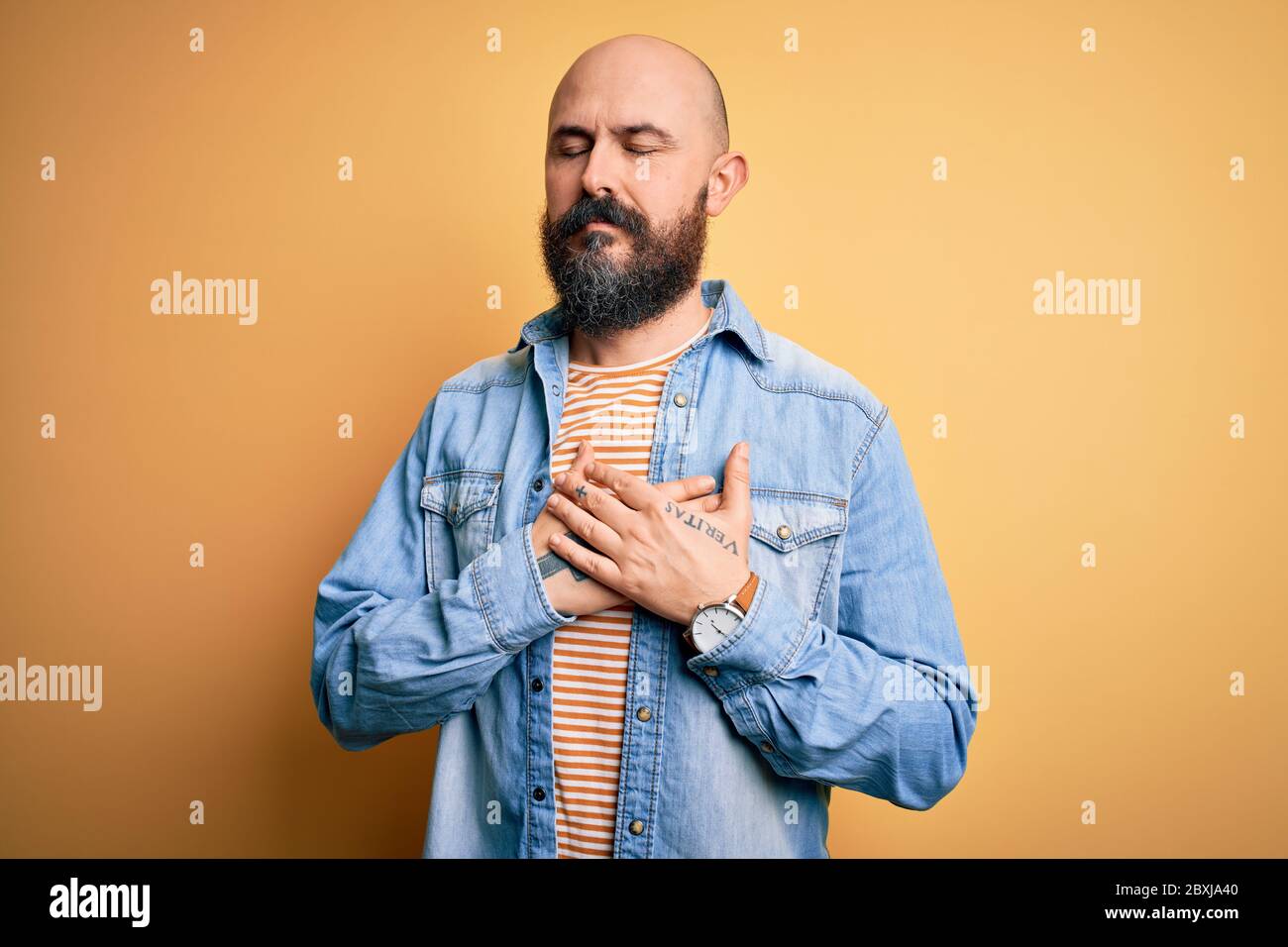 Handsome bald man with beard wearing casual denim jacket and striped t ...
