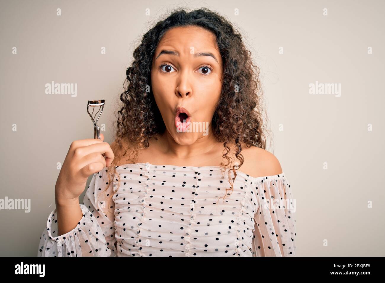 Young beautiful woman with curly hair holding eyelases curler over ...