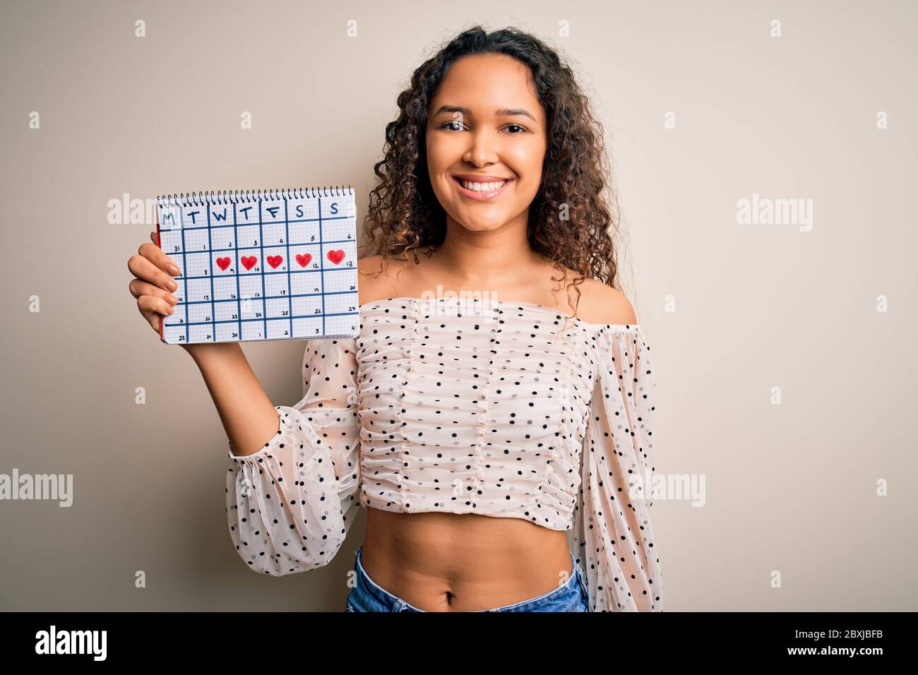 Young beautiful woman with curly hair holding mensturation calendar ...