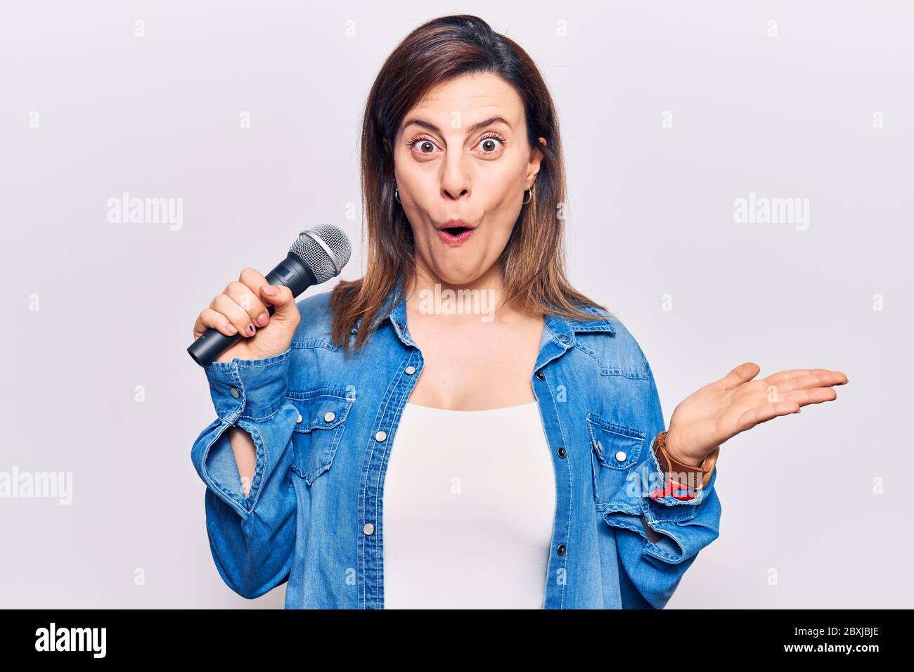 Young beautiful woman singing song using microphone scared and amazed ...