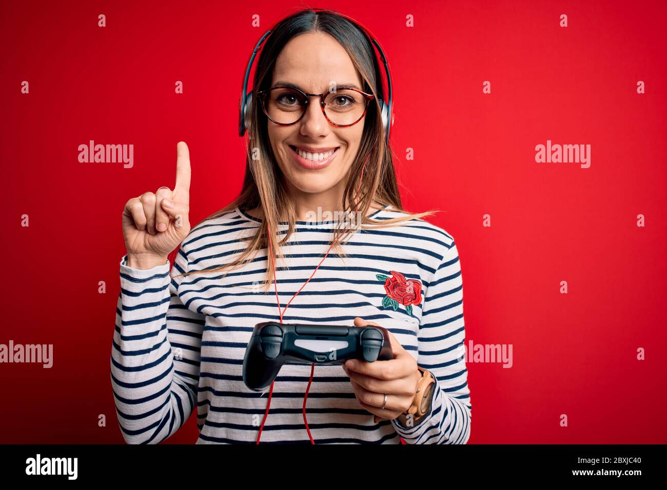 Young blonde gamer woman using gamepad playing video games over red ...
