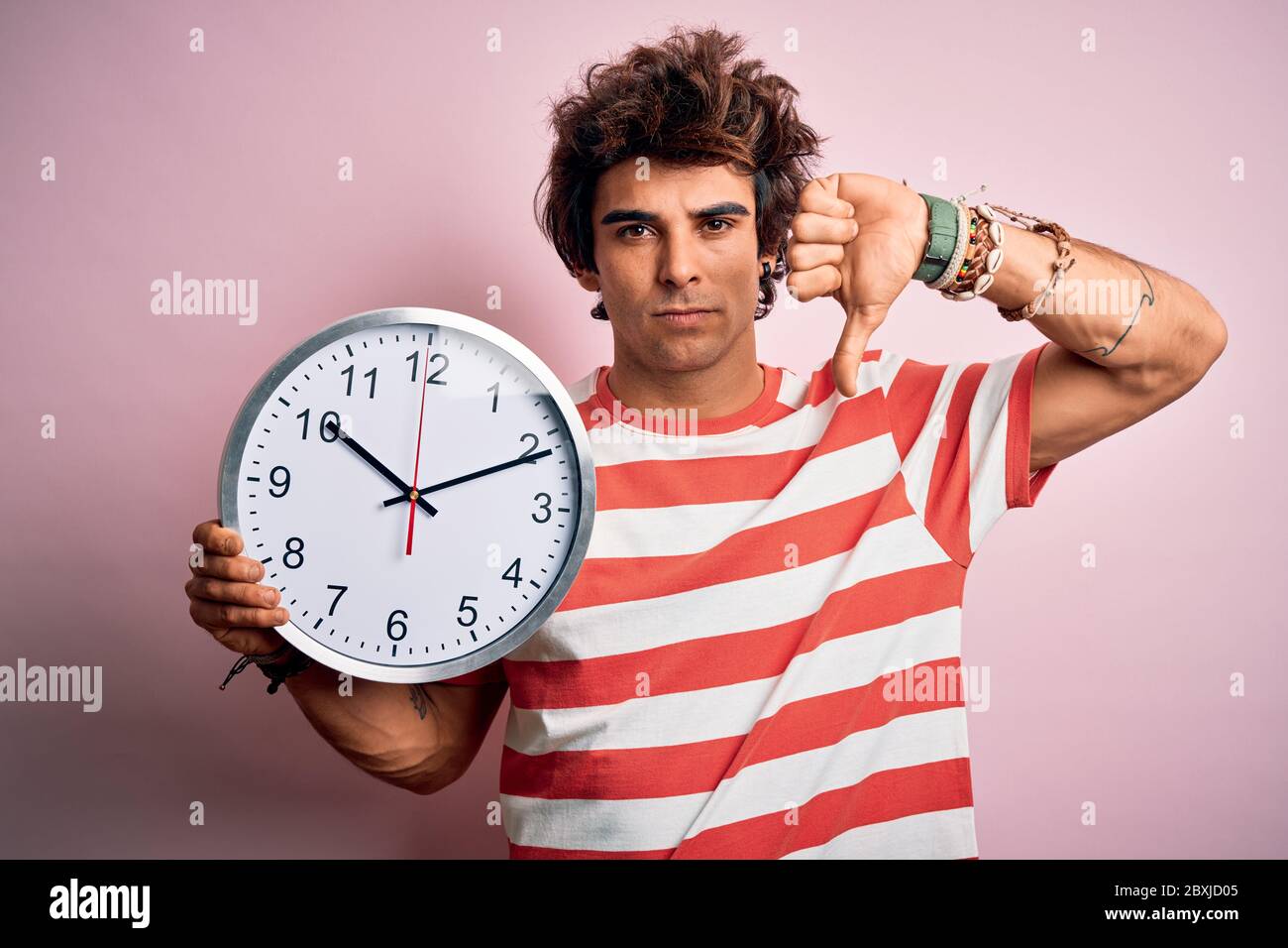 Young handsome man holding big clock standing over isolated pink ...