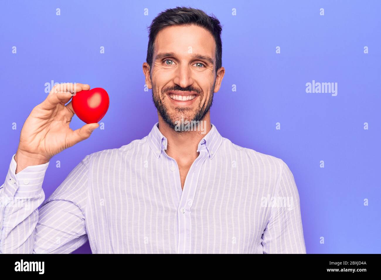 Young handsome man asking for health care holding red heart over ...