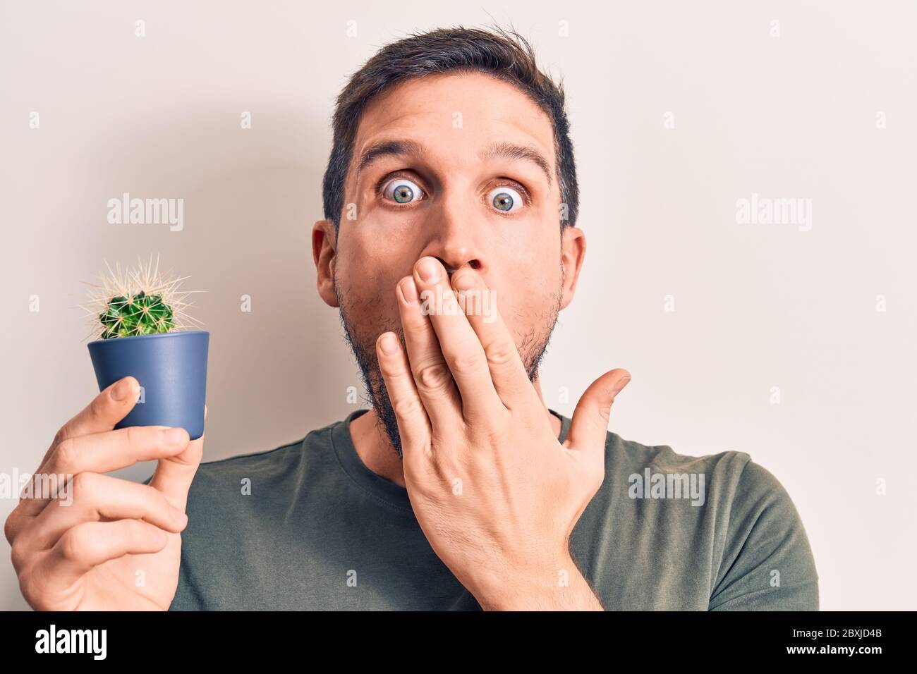 Young handsome man holding small cactus plant pot over isolated white ...