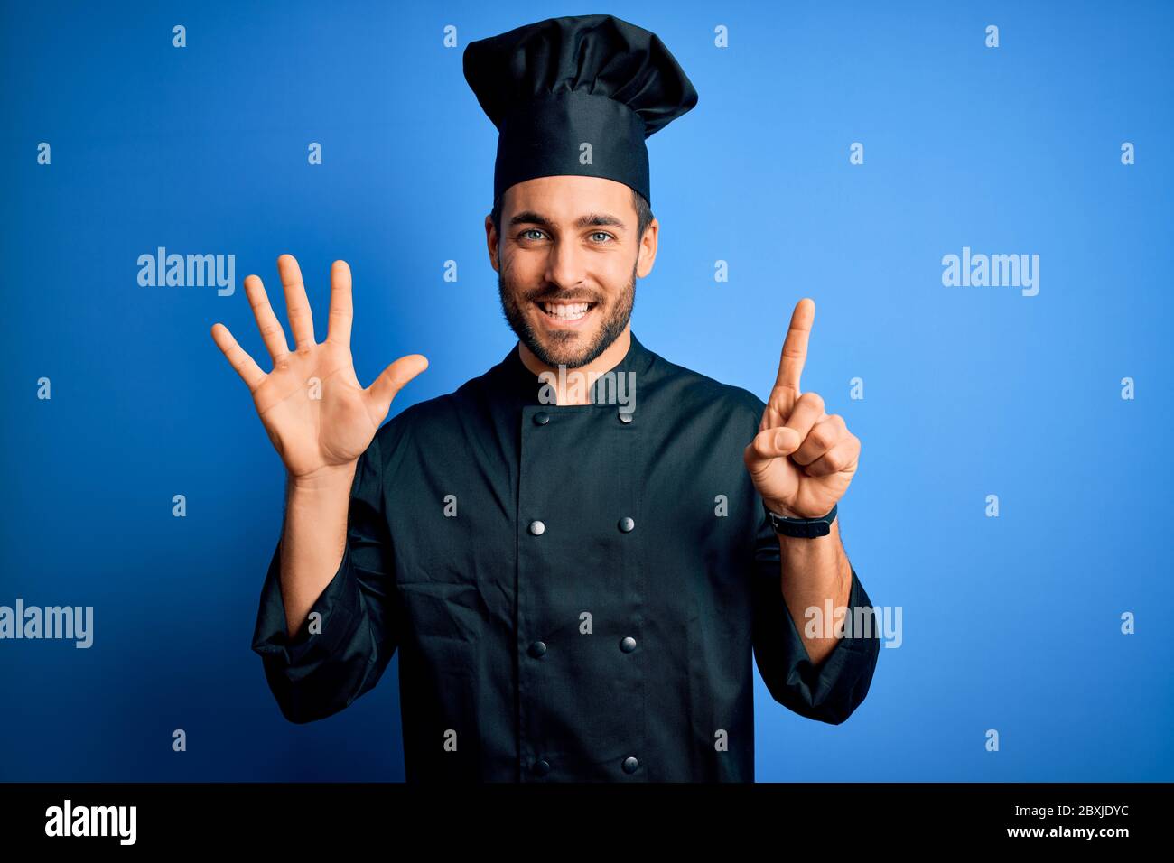 Young handsome chef man with beard wearing cooker uniform and hat over ...