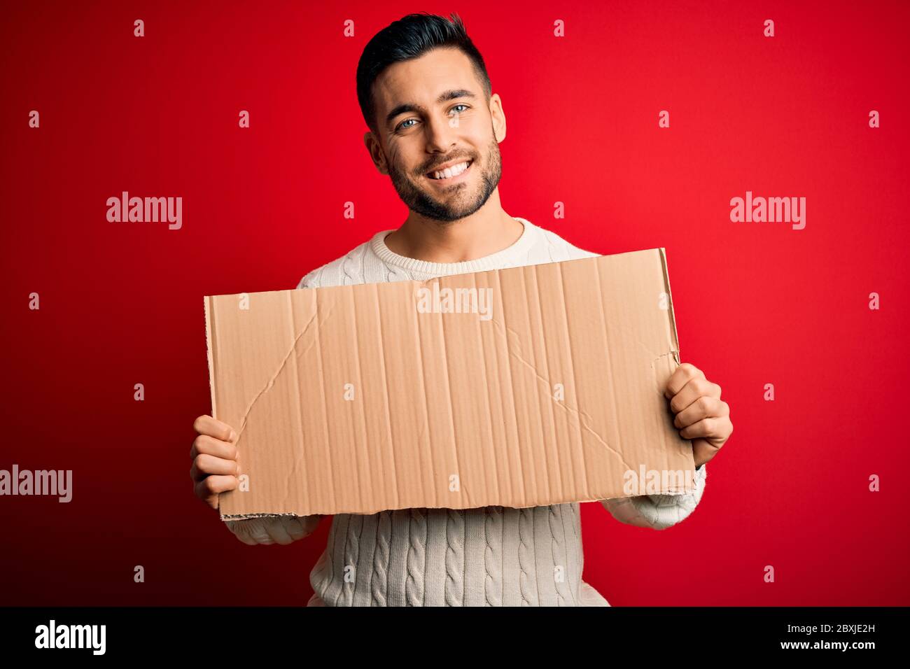 Young handsome man holding blank cardboard banner over isolated red ...