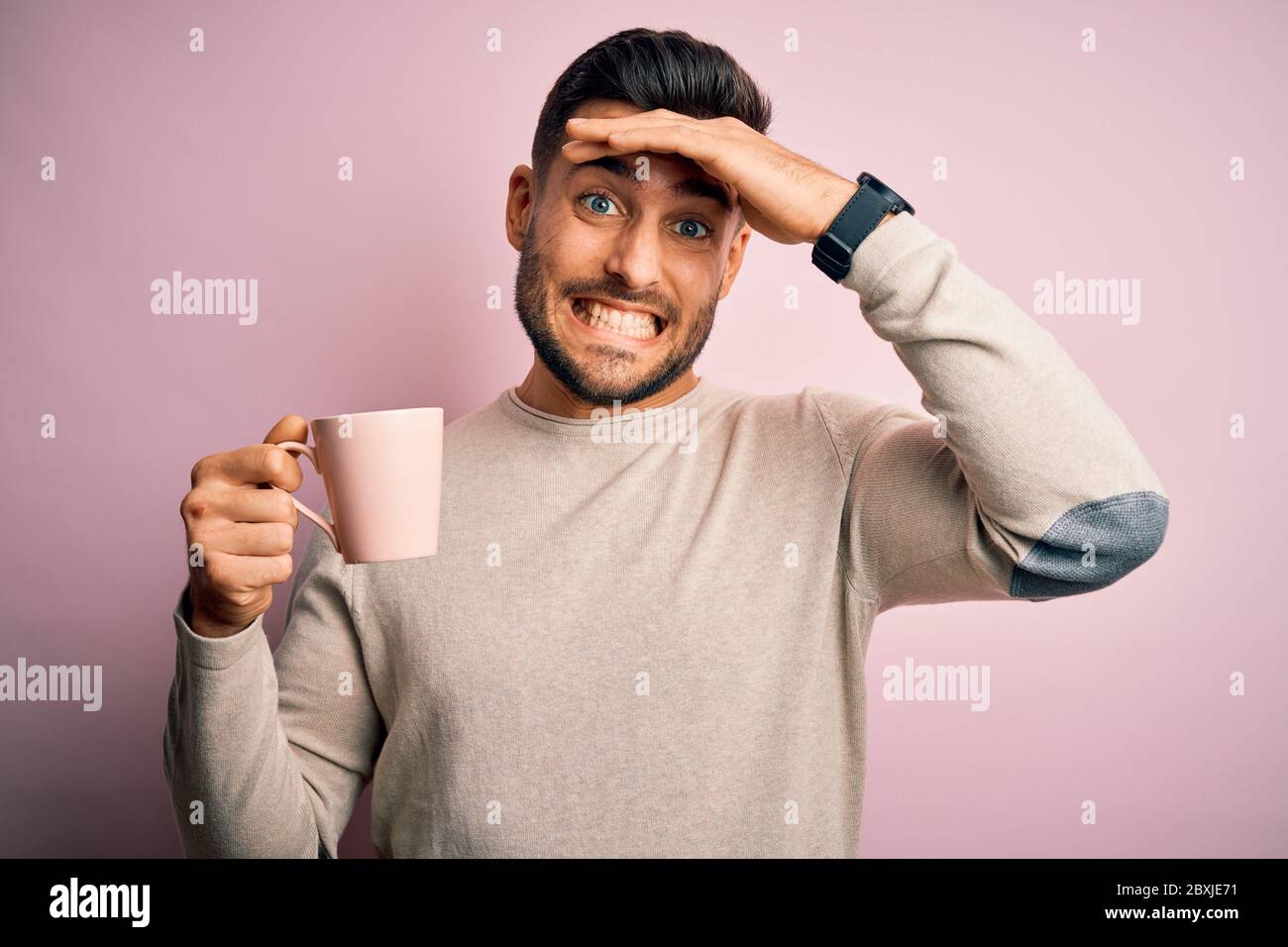 Young handsome man drinking a cup of hot coffee over pink isolated ...