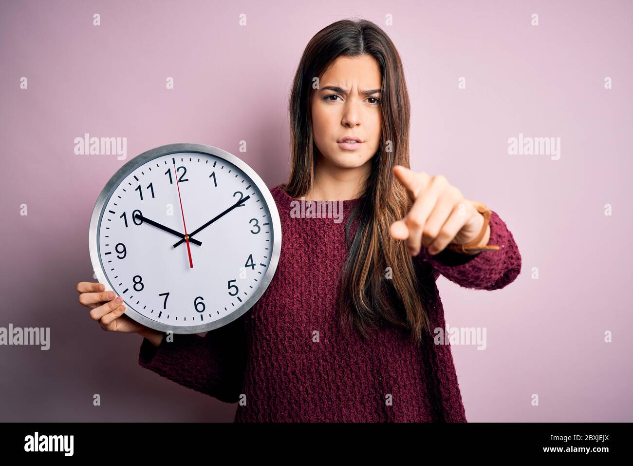 Young beautiful girl doing countdown holding big clock over isolated ...