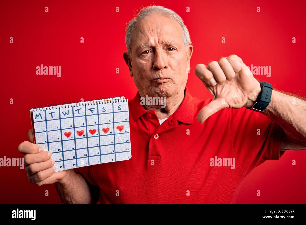 Senior grey haired man holding special date calendar over red ...