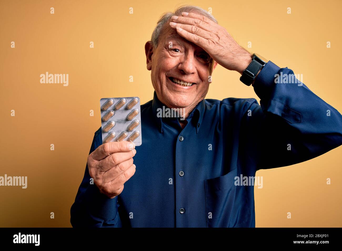 Senior grey haired man holding pharmaceutical pill drugs over yellow ...