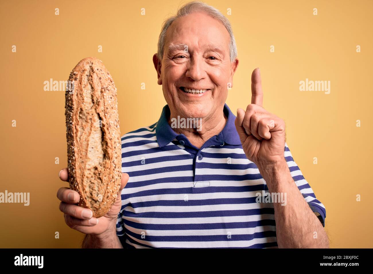 Grey haired senior man holding healthy wholemeal bread over yellow ...