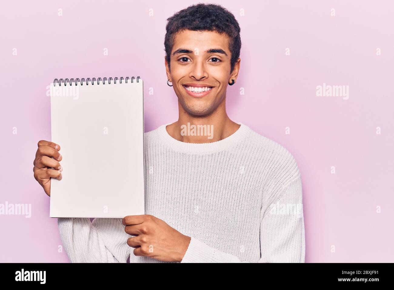 Young african amercian man holding notebook looking positive and happy ...