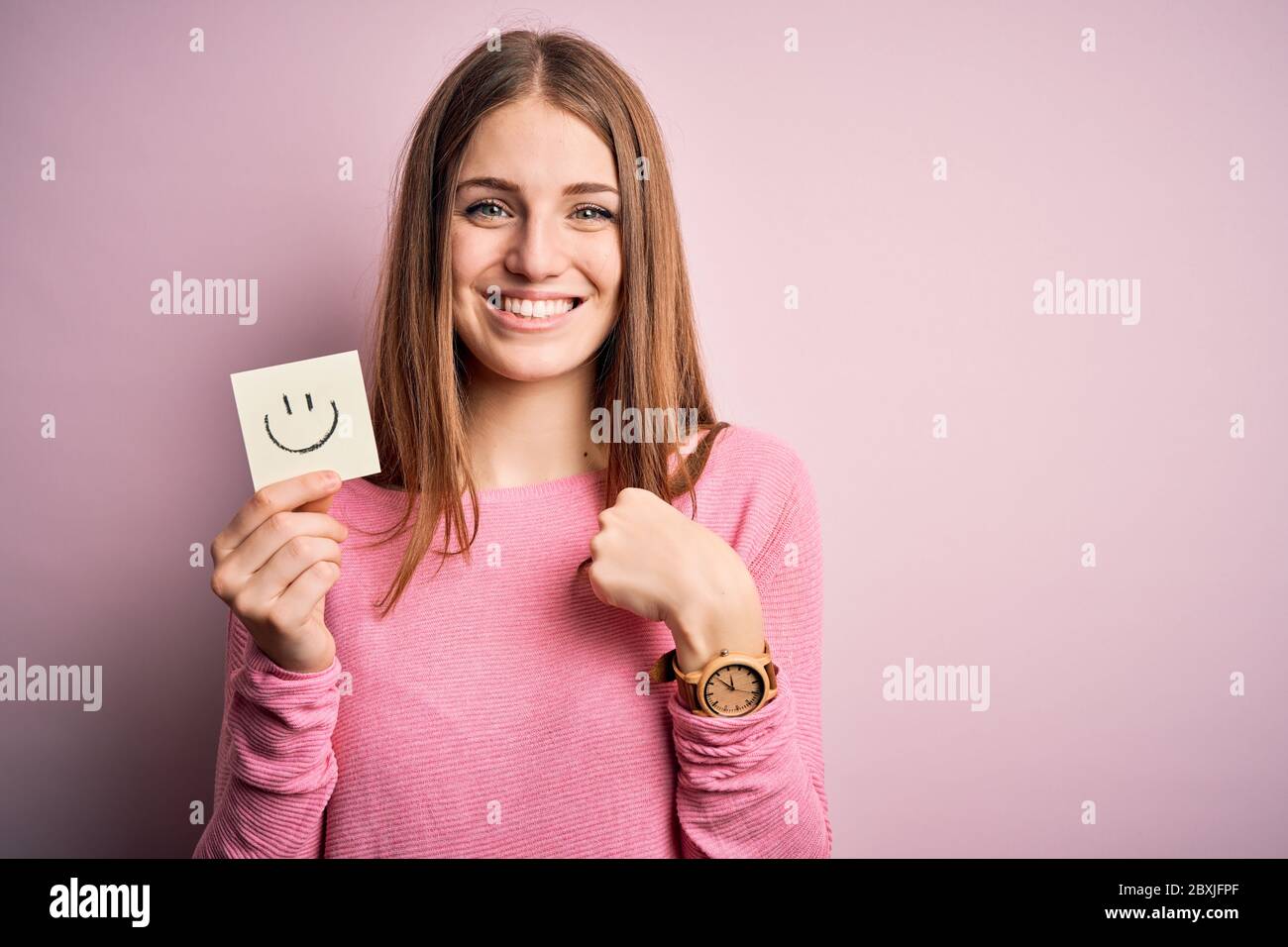 Young beautiful redhead woman holding reminder paper with smile emoji ...