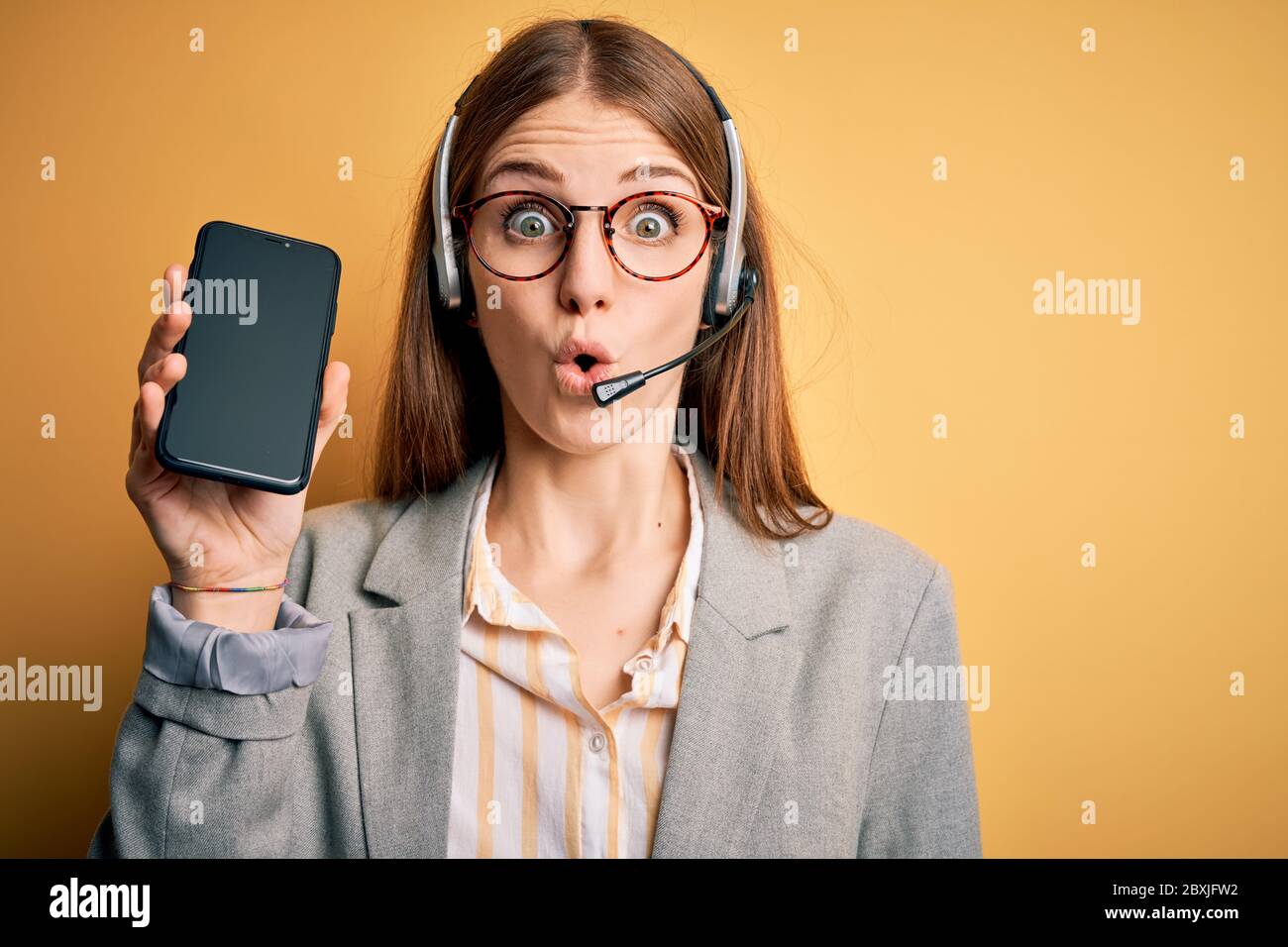 Young redhead call center agent woman using headset holding showing ...