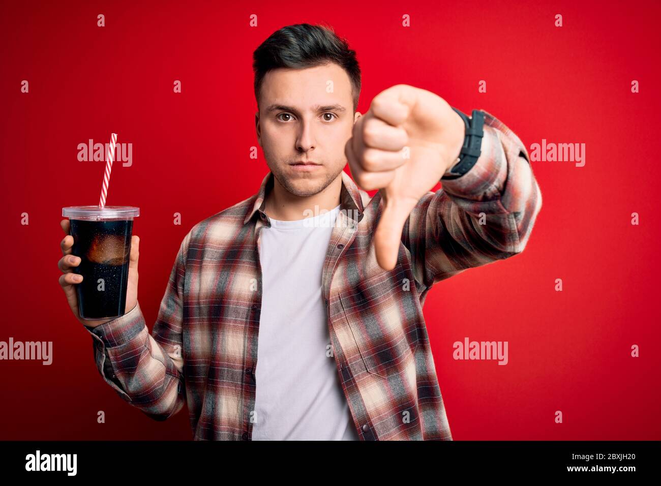 Young handsome caucasian man drinking a fresh soda refreshment over red ...
