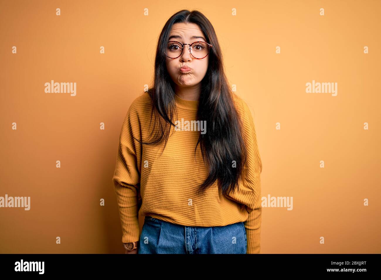 Young brunette woman wearing glasses and casual sweater over yellow ...