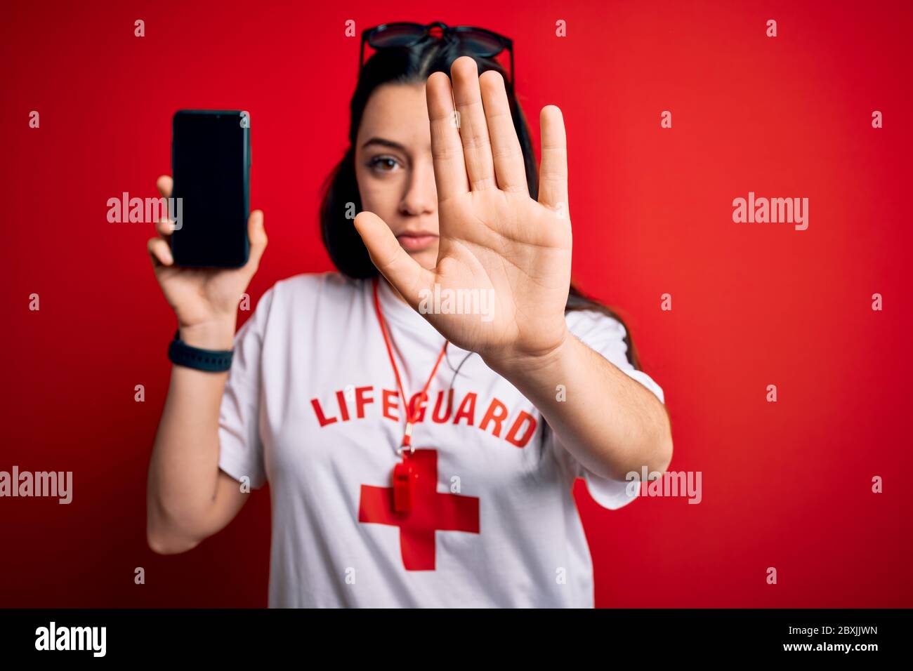 Young lifeguard woman showing smartphone screen over red background ...
