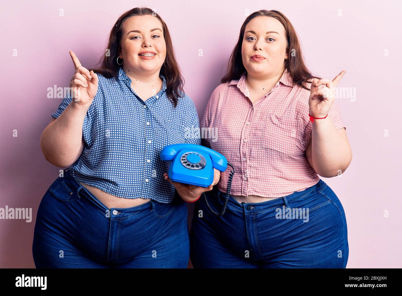 Young plus size twins holding vintage telephone smiling happy pointing ...