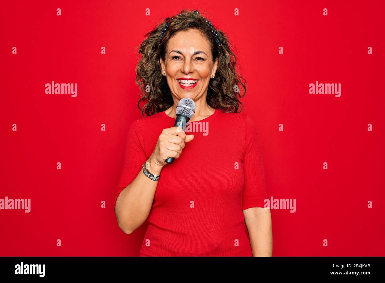 Middle age senior singer woman singing using music microphone over red ...